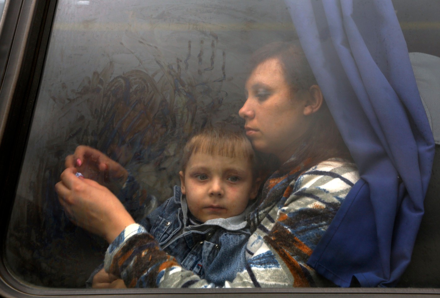 Ukrainian civilians inside a bus look at the remains of a burnt out ...